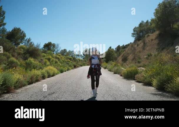 Free spirited woman with a backpack walking along a mountain road and ...