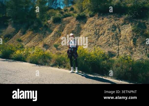 Free spirited woman with a backpack walking along a mountain road and ...