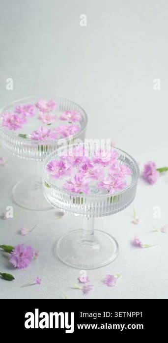 Two glasses of water with floating pink flowers on a light surface ...