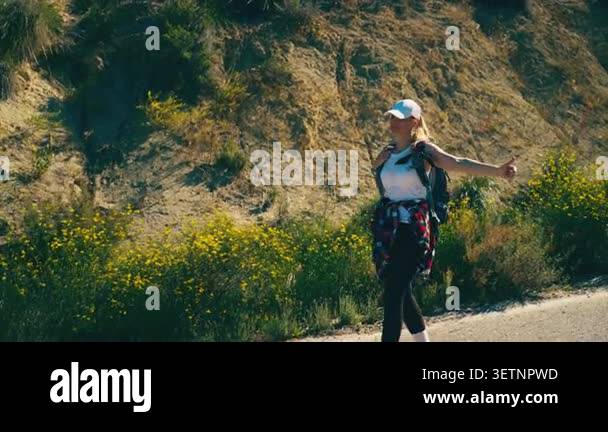 Free spirited woman with a backpack walking along a mountain road and ...