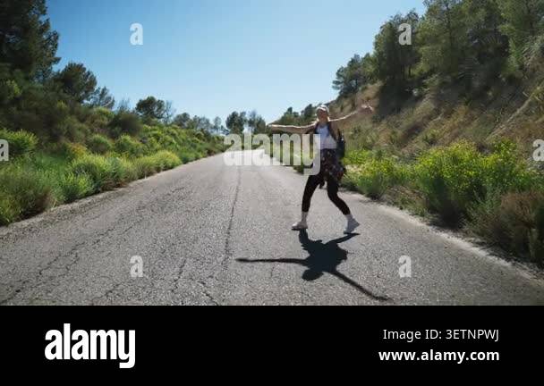 Free spirited woman with a backpack walking along a mountain road and ...