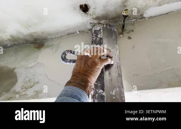 Male hand uses a putty knife to apply and spread fresh putty on ...