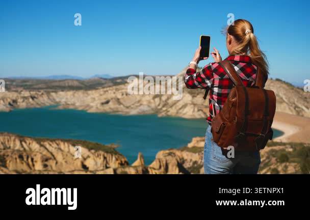 woman with backpack taking pictures of the camera on the mountain lake ...