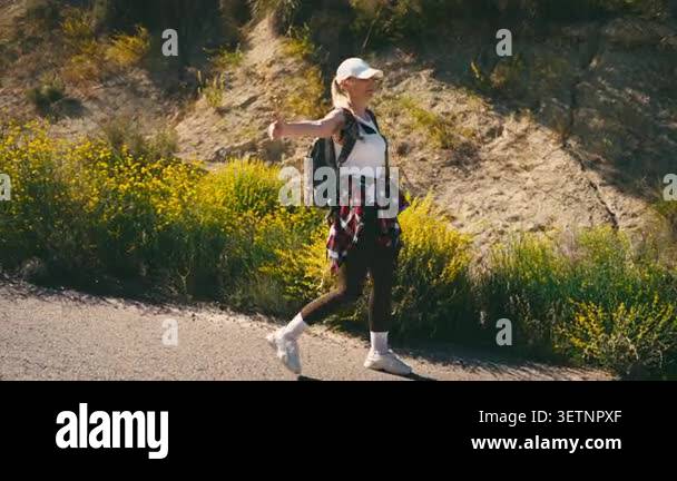 Free spirited woman with a backpack walking along a mountain road and ...