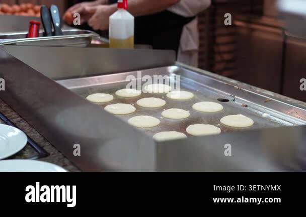 Fresh pancakes cooking on hot flat top griddle in professional ...