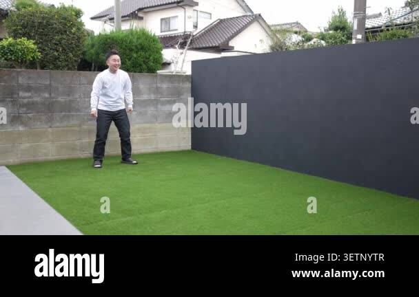 Man standing on green grass near wall and playing with ball on backyard ...