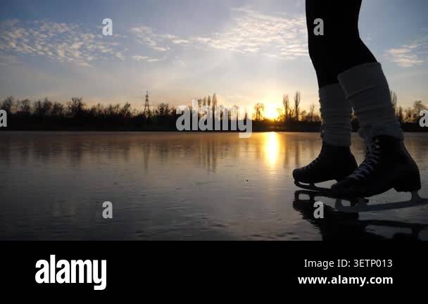 Female feet of skater skating on frozen river at beautiful sunset. Legs ...
