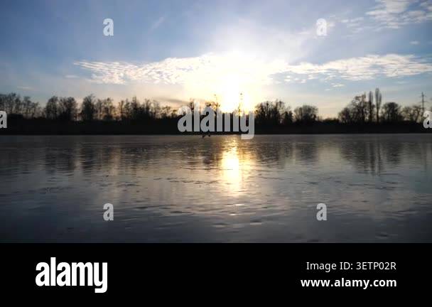 Young man skating on frozen river during sunset time. Guy shod in ...