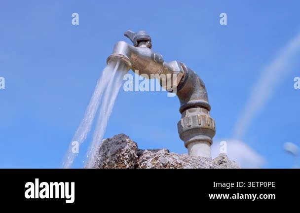 Metal water faucet with a flowing stream of clean water against a ...