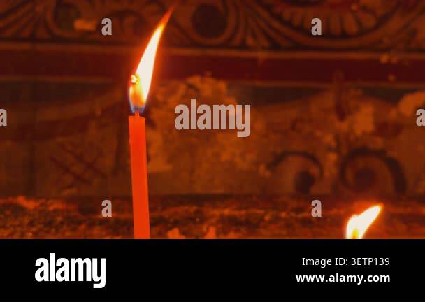 Glowing orange candle flame burning in a dim church interior, peaceful ...