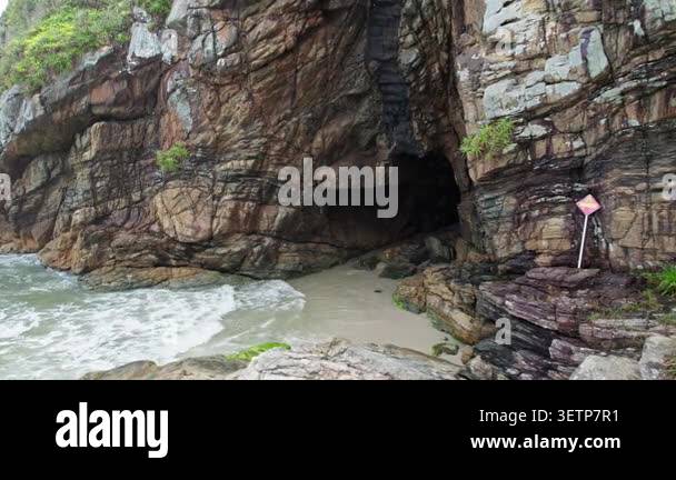 Reveal of a stunning sea cave entrance from a bay with ocean waves on a ...