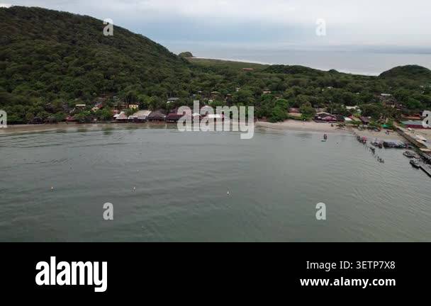 Aerial view of a serene beach village nestled between lush green hills ...