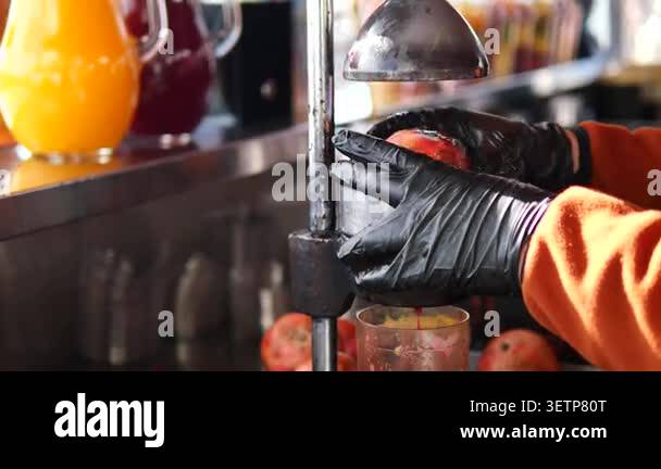 Hands prepare fresh juice using a fruit press in a busy kitchen setup ...