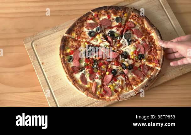 A round pizza sits on a wooden board with different toppings and slices ...