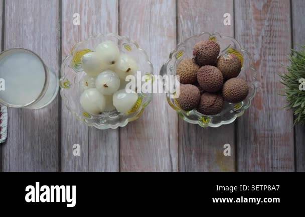 Two bowls hold lychee and longan fruits on a wooden table surface Stock ...
