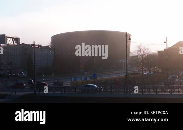 Urban sunset street view centered on large cylindrical arena. Ornate ...