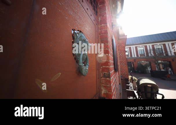 Close up of lion head door knocker on rusted door beside brick facade ...