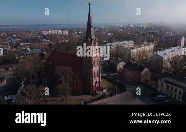 Aerial focus on red brick Gothic church with tall spire and cross in a ...