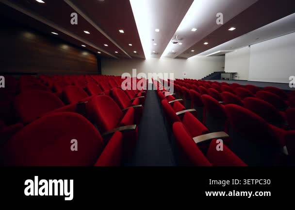 Empty lecture hall with red seats, wood wall, small stage, stairs ...