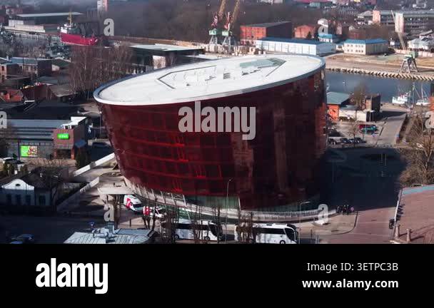 Aerial pan of red glass cultural building by quay with cranes, moored ...