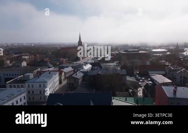Aerial drone pans over a Baltic town toward a tall red brick church ...
