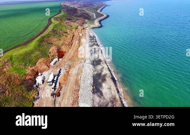 Excavator placing blocks on coastal seawall with sea and rock. Overhead ...
