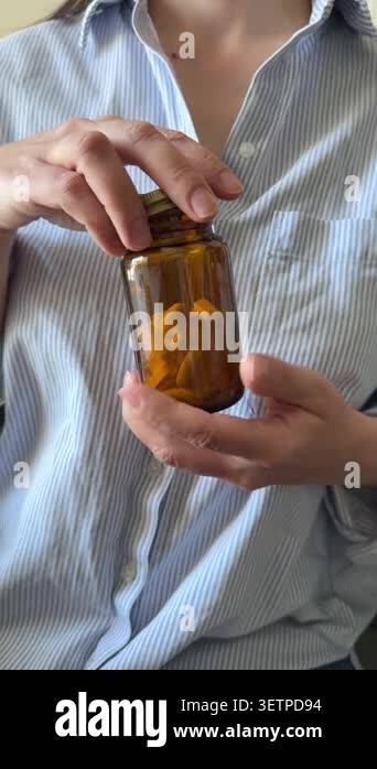 Woman opening small brown glass bottle with pills and taking two big ...