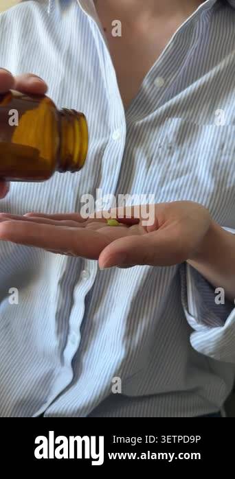 Woman pouring out one white pill from the glass jar to her hand with ...