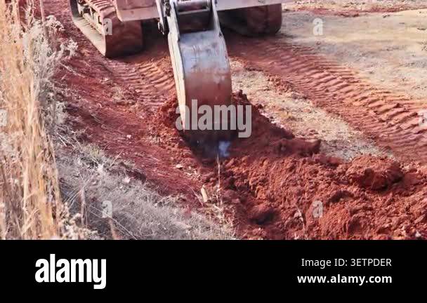 Heavy excavator machine digs into red soil on construction site during ...