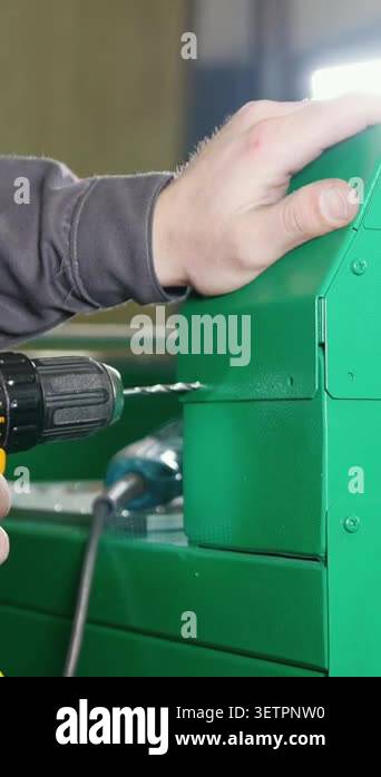 Worker man using an electric hand drill - making hole in green metal ...