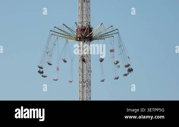 High swing ride spinning and climbing a tower against a clear blue sky ...