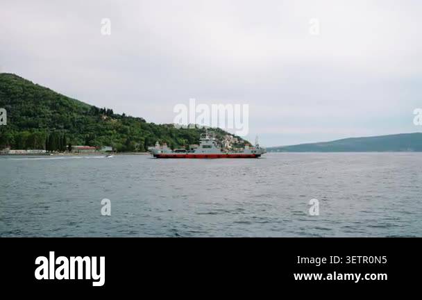 Supply vessel crossing calm grey sea with green hillside village ...