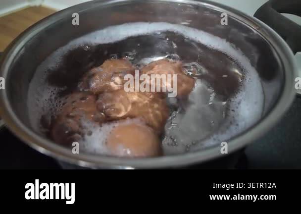 Close-up of chicken eggs boiling in stainless pan with hot water and ...