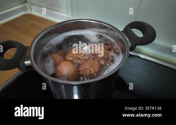 Close-up of chicken eggs boiling in stainless pan with hot water and ...