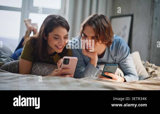 Modern couple looking cellphone lying together at bed loft apartment ...
