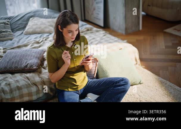 Peaceful brunette reading mobile phone message sitting carpet in cozy ...