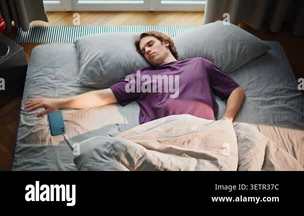 Awaking man checking alarm lying mattress in light apartment closeup ...