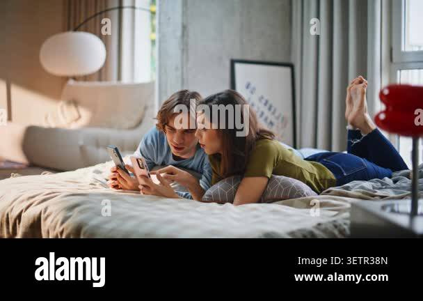 Teen lovers using smartphones chilling loft bedroom. Young positive ...