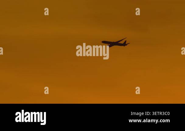 Passenger airplane silhouette flying across a vibrant golden orange sky ...