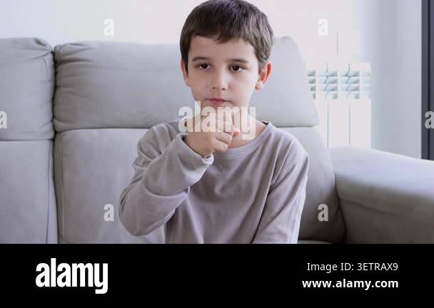 Child sitting on sofa at home and holding hand on chest. Male having ...