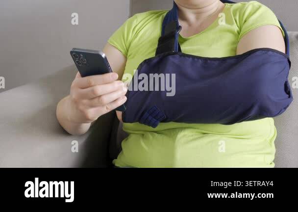 Close up of woman hands with broken arm wearing sling using smart phone ...
