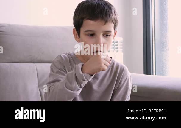 Child sitting on sofa at home and holding hand on chest. Male having ...