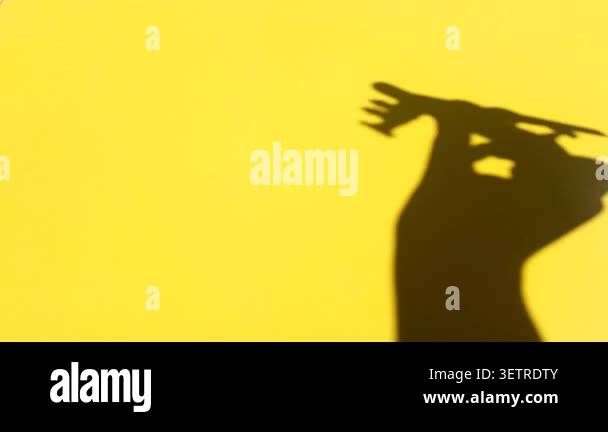 A hand holding a toy airplane casts a dramatic shadow on a vivid yellow ...
