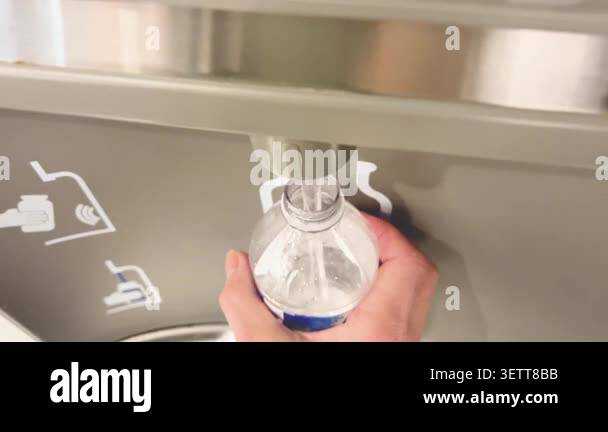 A person holds a plastic water bottle under a water fountain spout to ...