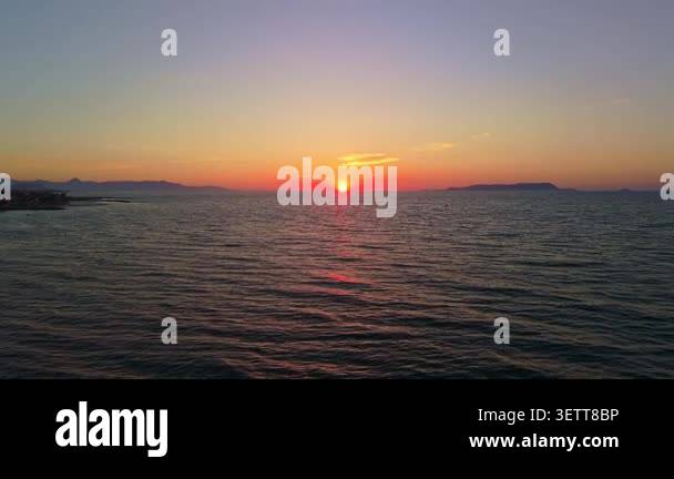 Cinematic drone footage capturing a vibrant orange sun rising directly ...