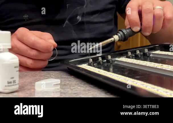 Hands work diligently on a circuit board, soldering tiny components ...