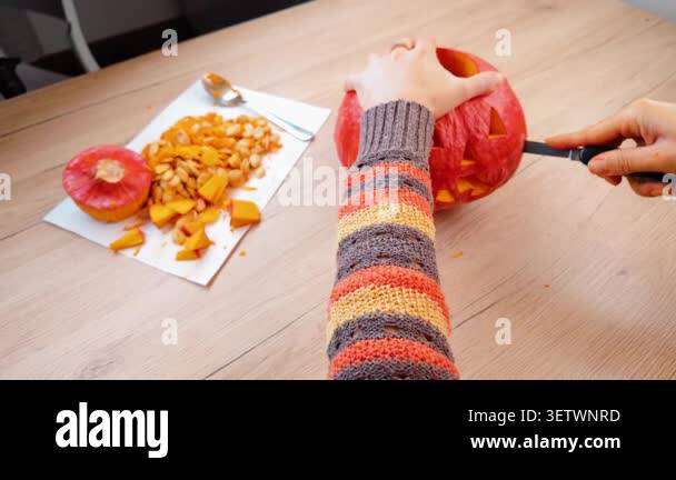 Female hands carving a Jack o lantern on a wooden table for the autumn ...