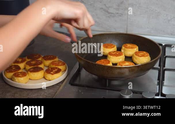 Woman's hands using a fork to move freshly cooked syrniki from a hot ...