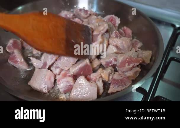 Pork pieces sizzling in a hot stainless steel frying pan while being ...