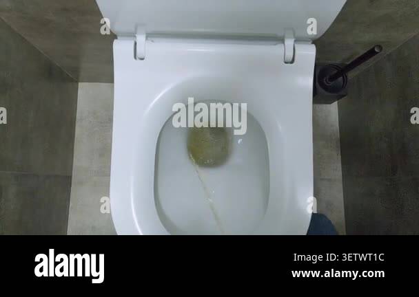 Top-down view of urine stream filling a clean white ceramic toilet bowl ...